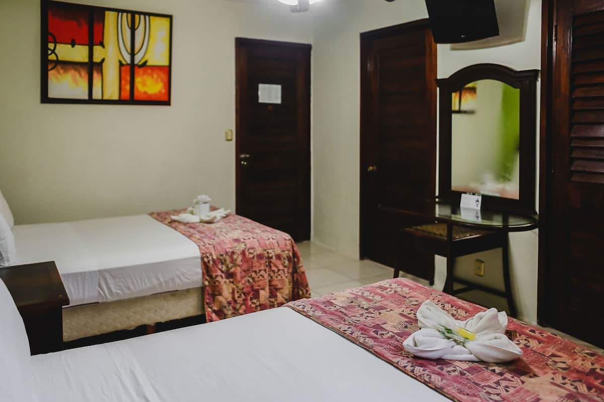 Quarto de hotel com duas camas, penteadeira de madeira, espelho e um quadro na parede.