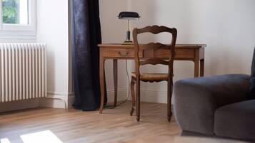 Uma mesa de madeira com uma lâmpada, uma cadeira e um radiador num quarto com soalho de madeira e uma janela com cortinas.