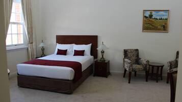 Quarto de hotel com uma cama grande, duas mesas de cabeceira, uma cadeira, uma mesinha e um quadro na parede.