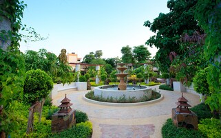 Um jardim com uma fonte central, ladeado por caminhos de pedra e vegetação.