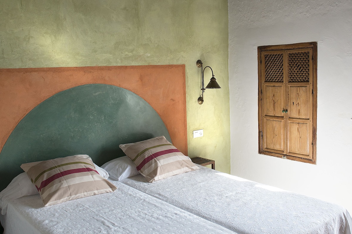 Quarto com duas camas, um guarda-roupa de madeira, uma luminária na parede e parede com textura.