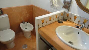 Um banheiro com vaso sanitário, bidê, pia e espelho.