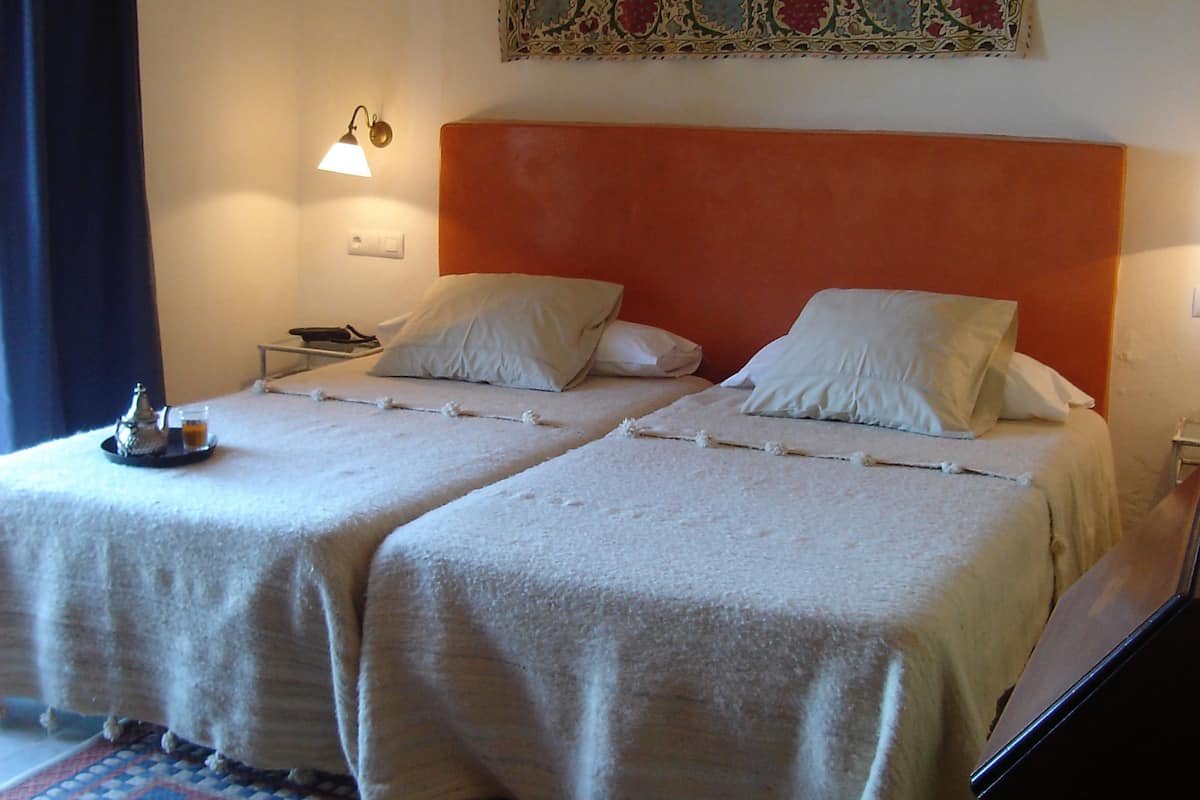 Cama de casal com cabeceira, mesa de cabeceira, abajur e tapete estampado.