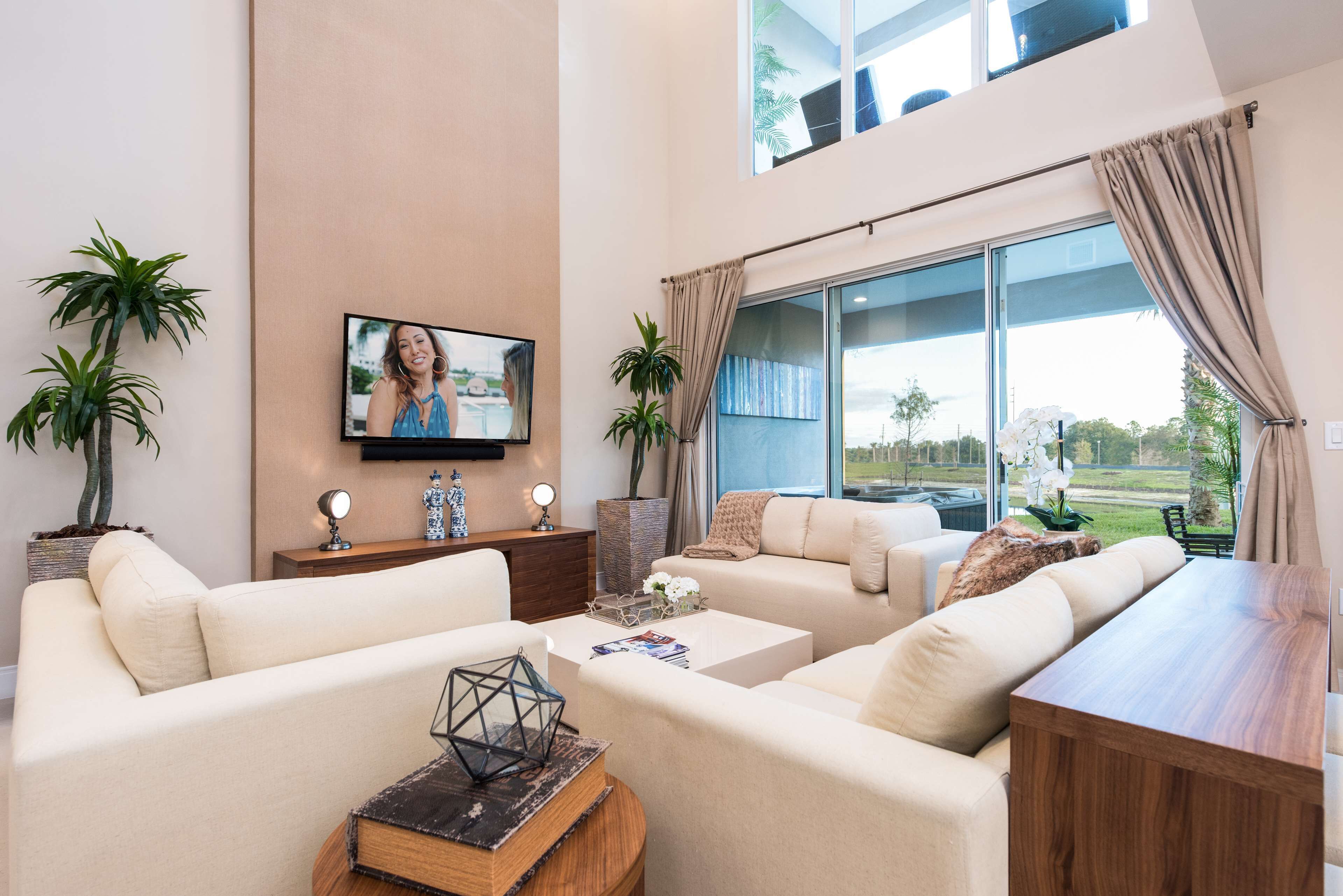 Uma sala de estar moderna com uma televisão grande, sofás confortáveis, uma mesa de centro e janelas amplas com cortinas.