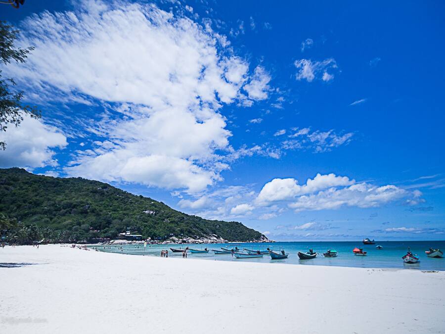 Uma praia com areia branca, águas azul-claras e barcos.