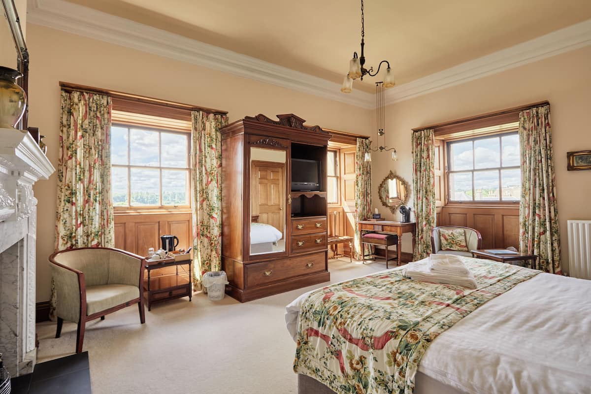 Quarto com uma cama grande, penteadeira de madeira, uma cadeira, escrivaninha e lareira.