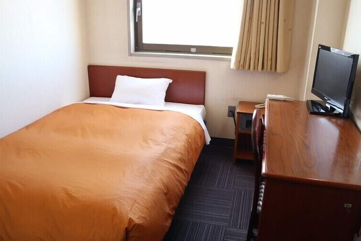 Quarto de hotel com cama, televisão, secretária e janela.