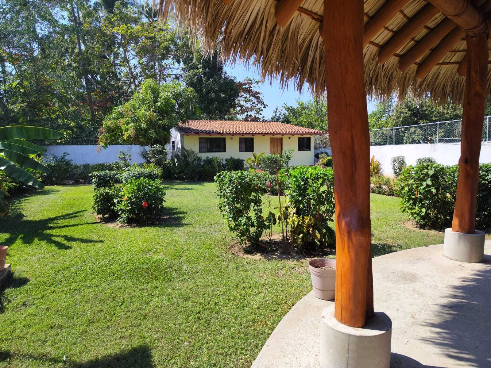 Uma casa com telhado de cerâmica, rodeada por um gramado bem cuidado e diversas plantas.