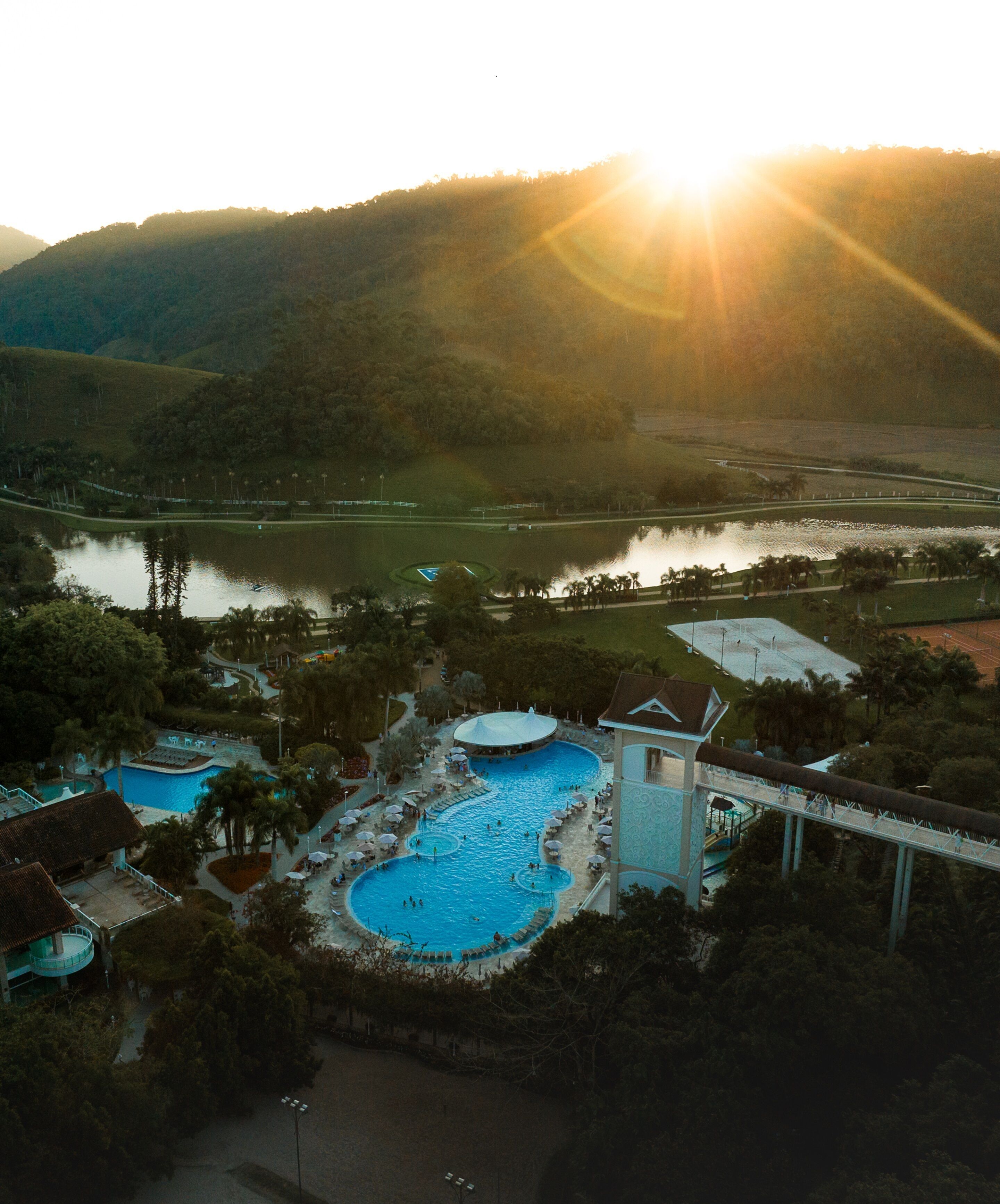 Um resort com várias piscinas, uma ponte e vista para um lago e montanhas.