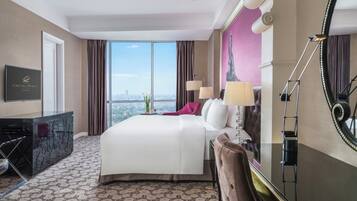 Quarto de hotel com uma cama grande, uma escrivaninha, uma cadeira, um espelho e vista para a cidade.