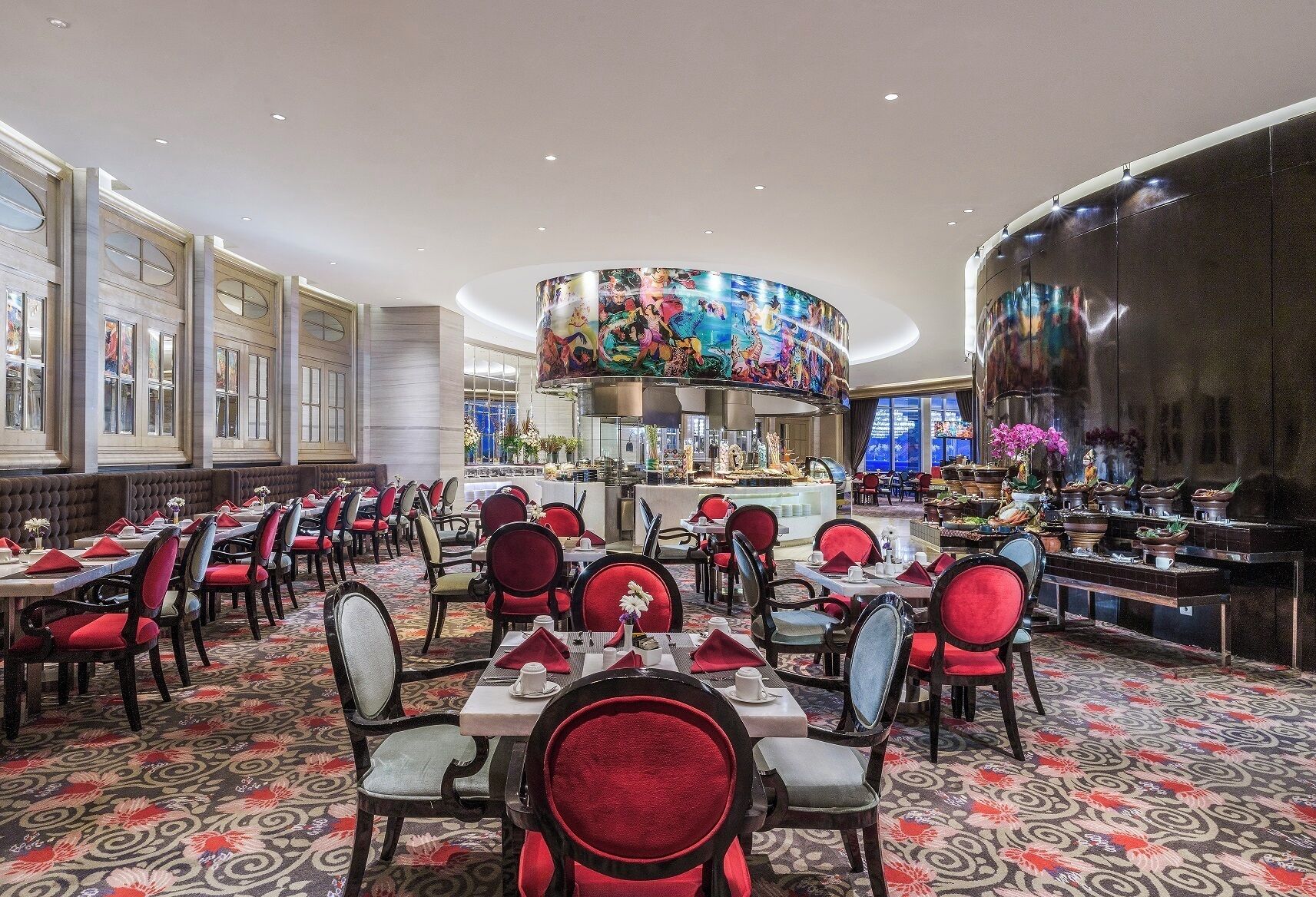 Restaurante com um balcão central, várias mesas de jantar com cadeiras vermelhas e cinzentas, e um tapete estampado.