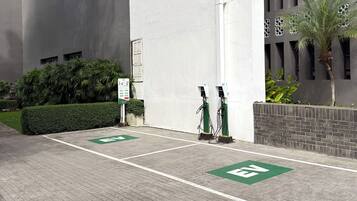 Uma área de estacionamento com estações de carregamento para veículos elétricos, uma placa e um edifício com design moderno.