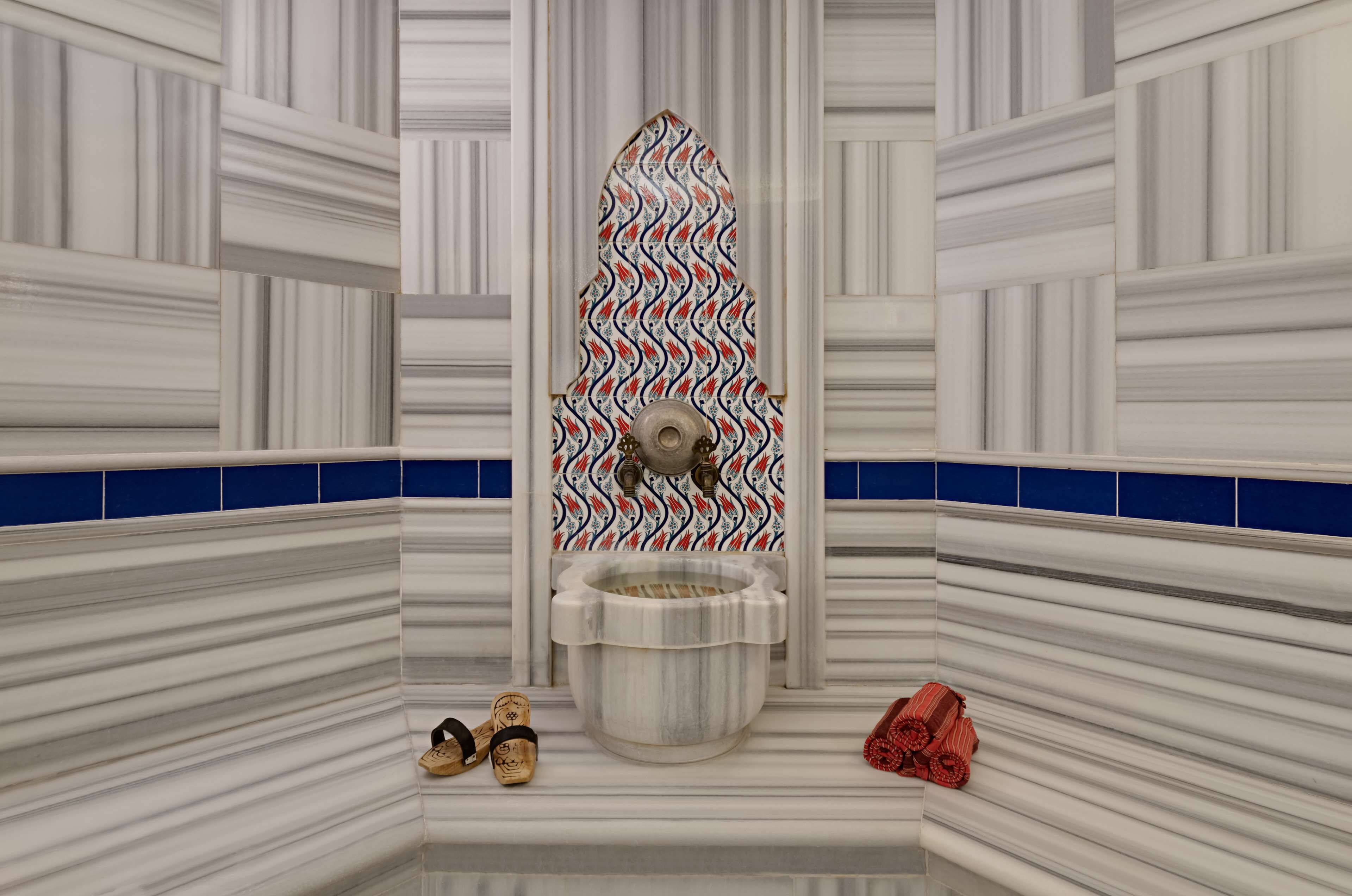 Um banheiro com pia de mármore, parede estampada e azulejos azuis.