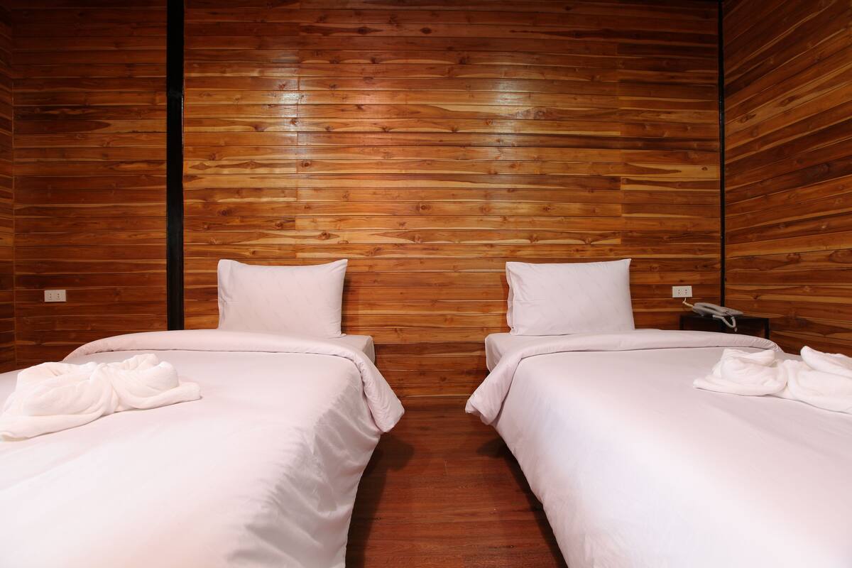 Quarto com duas camas, paredes de madeira e mesa de cabeceira com telefone.
