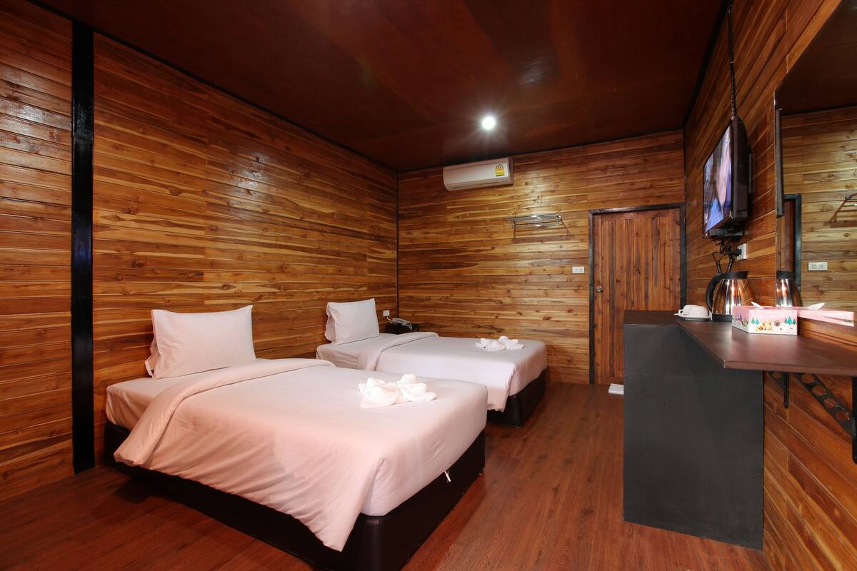 Quarto com painéis de madeira, duas camas, uma escrivaninha e uma televisão.