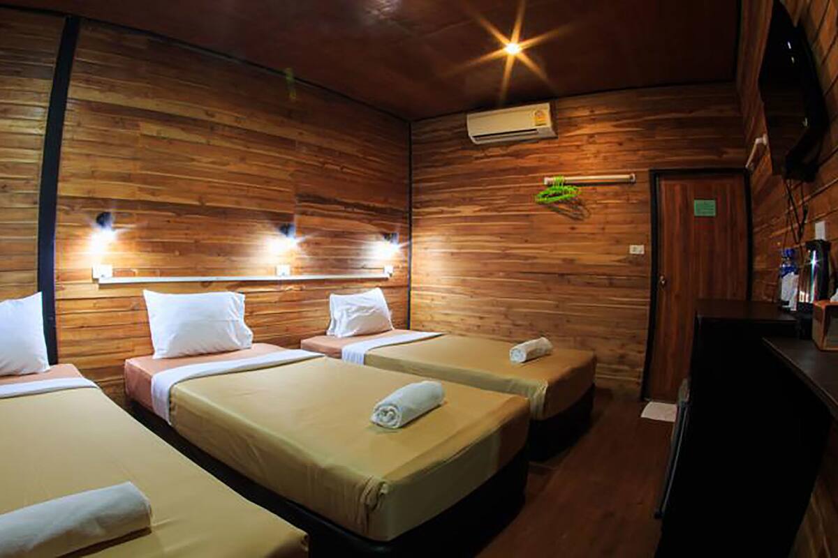 Quarto com quatro camas de solteiro, paredes de madeira, ar condicionado e uma escrivaninha com cadeira.