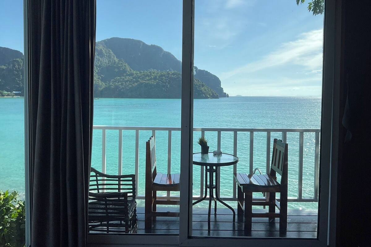 Uma varanda com vista para águas azul-turquesa e uma paisagem montanhosa.