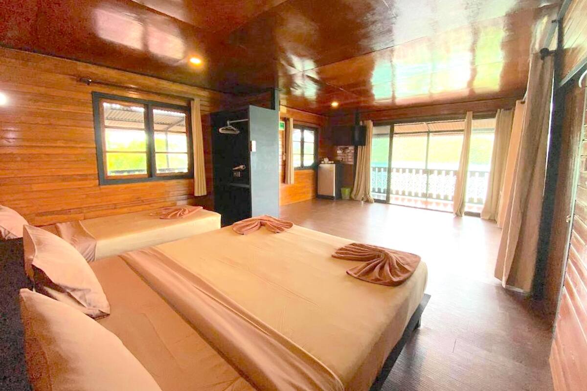 Quarto de hotel com duas camas, paredes de madeira, uma varanda e uma televisão.
