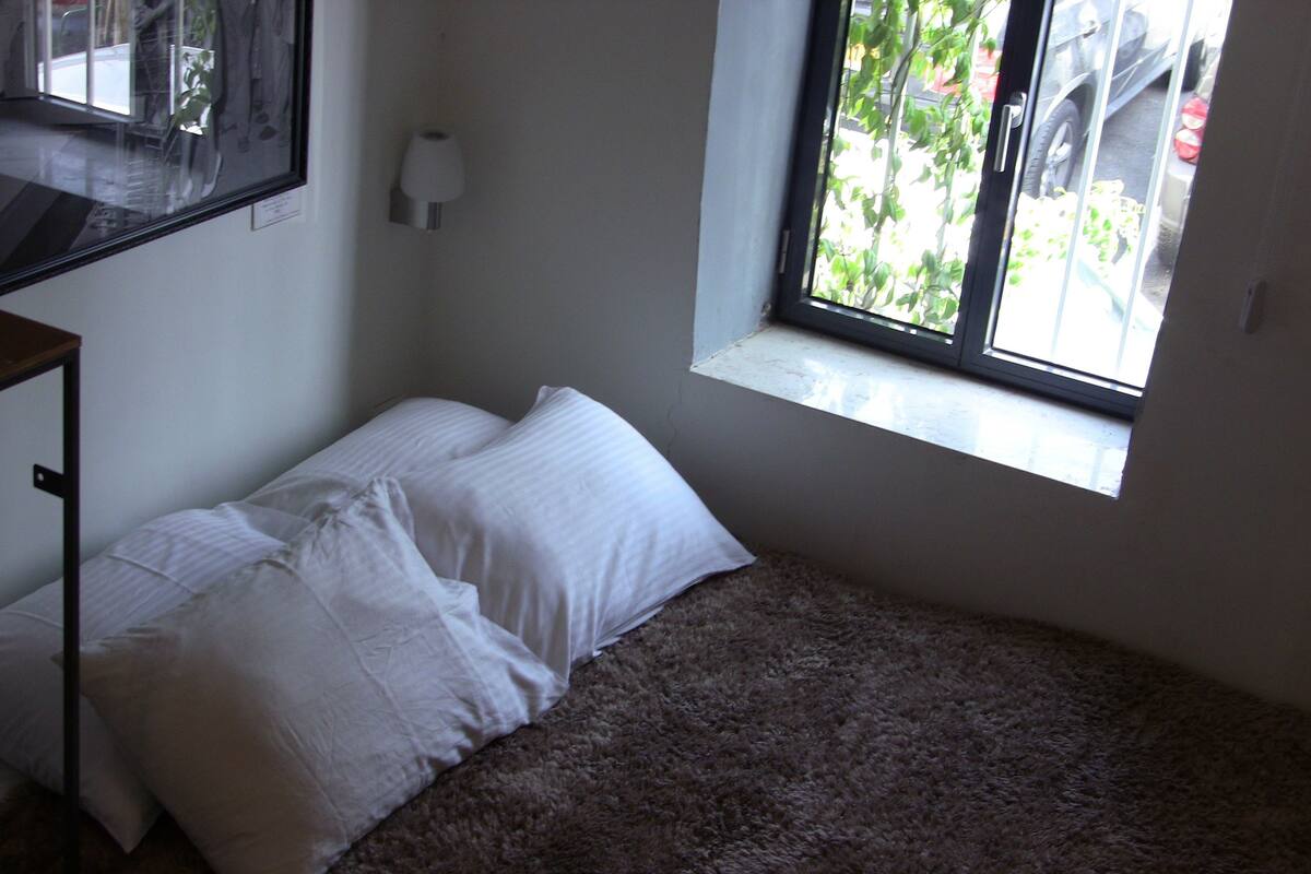 Quarto com cama, janela e luminária fixada na parede.