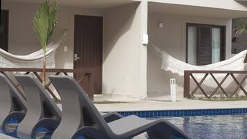 Área da piscina com espreguiçadeiras e rede.