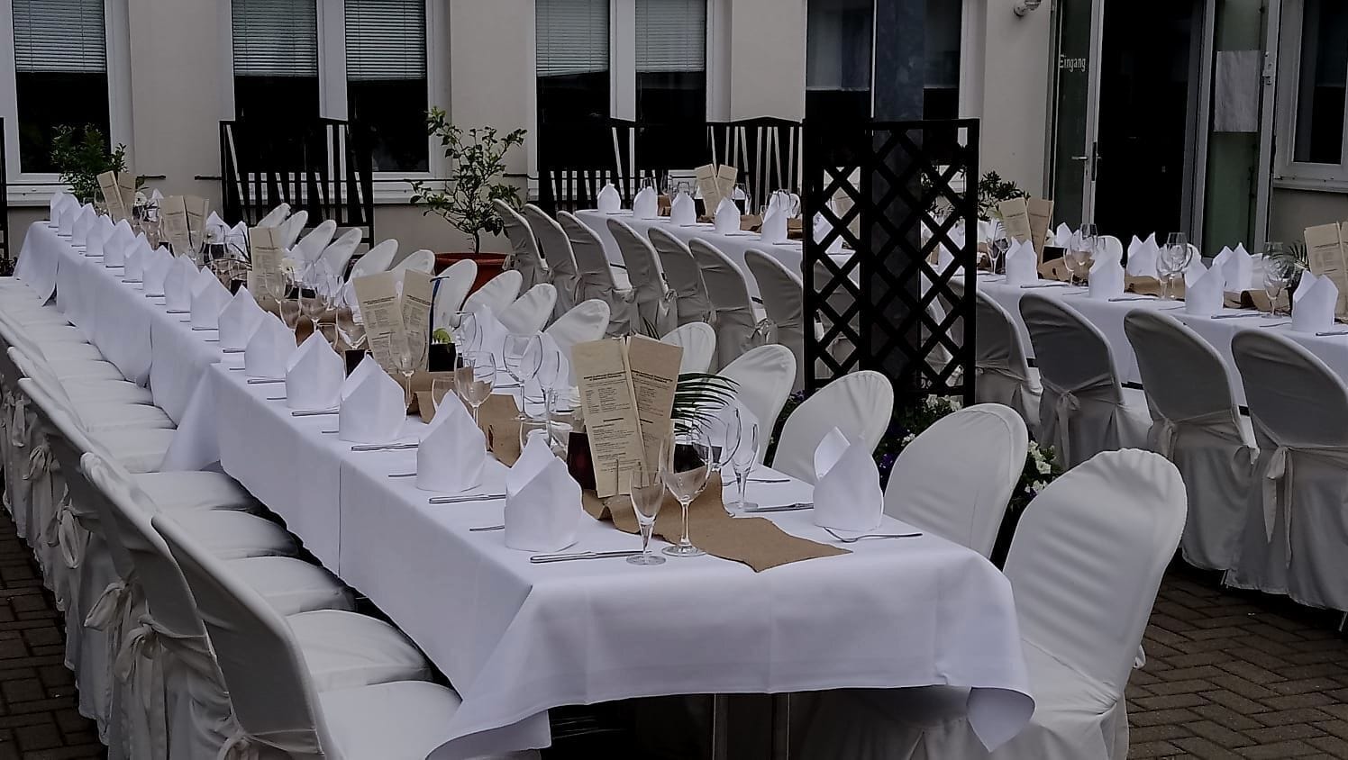 Uma longa mesa de banquete posta com toalhas brancas, cadeiras brancas e cartões de menu.