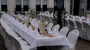 Uma longa mesa de banquete posta com toalhas brancas, cadeiras brancas e cartões de menu.