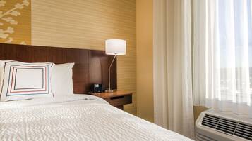 Quarto de hotel com cama, mesa de cabeceira com luminária, janela com cortinas e ar condicionado.