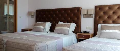 Quarto de hotel com duas camas, cada uma com cabeceira estofada, mesas de cabeceira e luminárias fixadas na parede.
