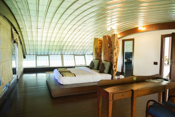 Quarto espaçoso com uma cama grande, uma escrivaninha de madeira e teto arredondado.