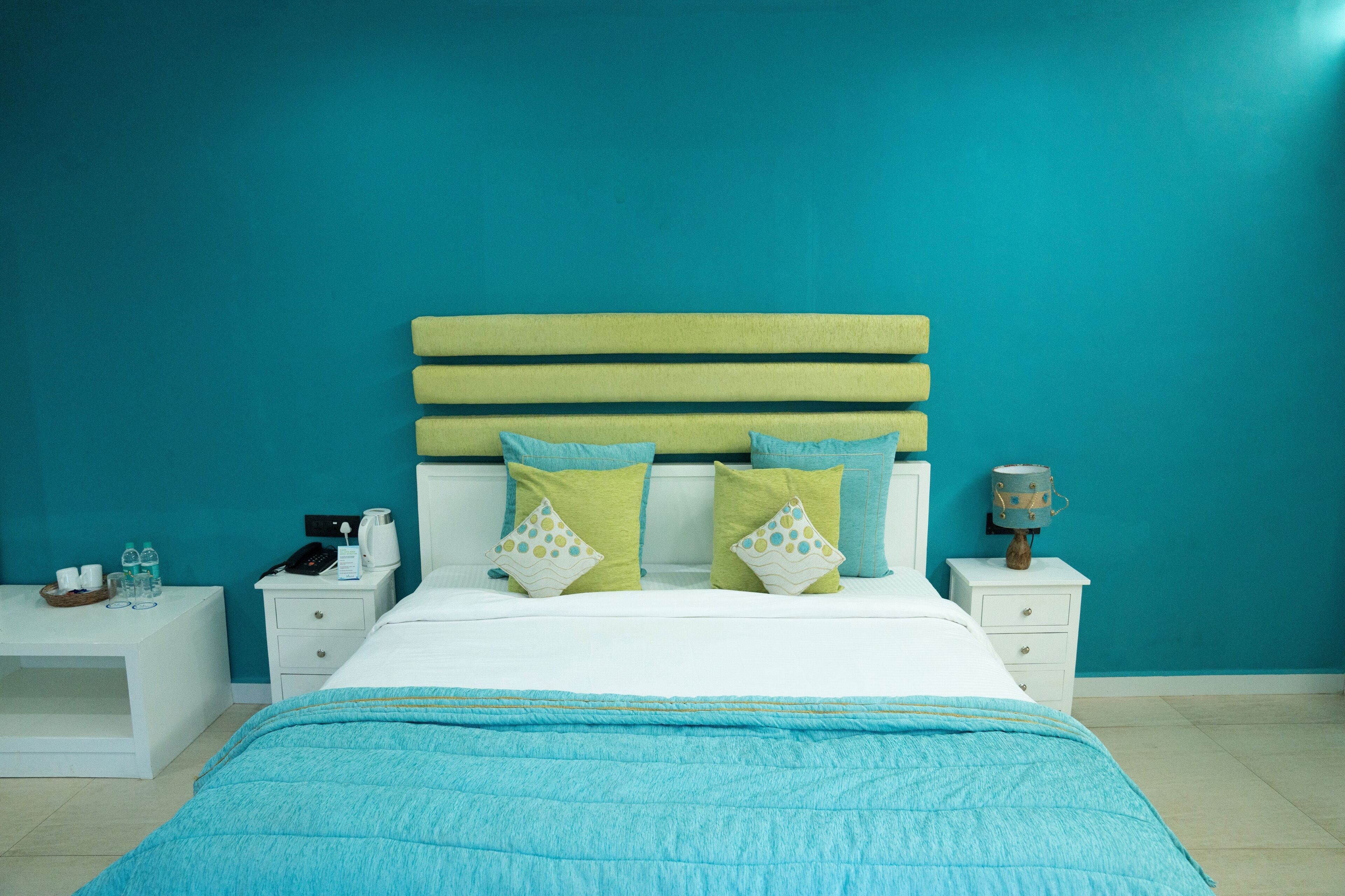 Um quarto com uma cama, duas mesas de cabeceira, um criado-mudo, uma luminária e um telefone fixado na parede.