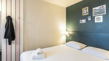 Quarto de hotel com cama, toalha, luminária fixada na parede e quadros emoldurados.