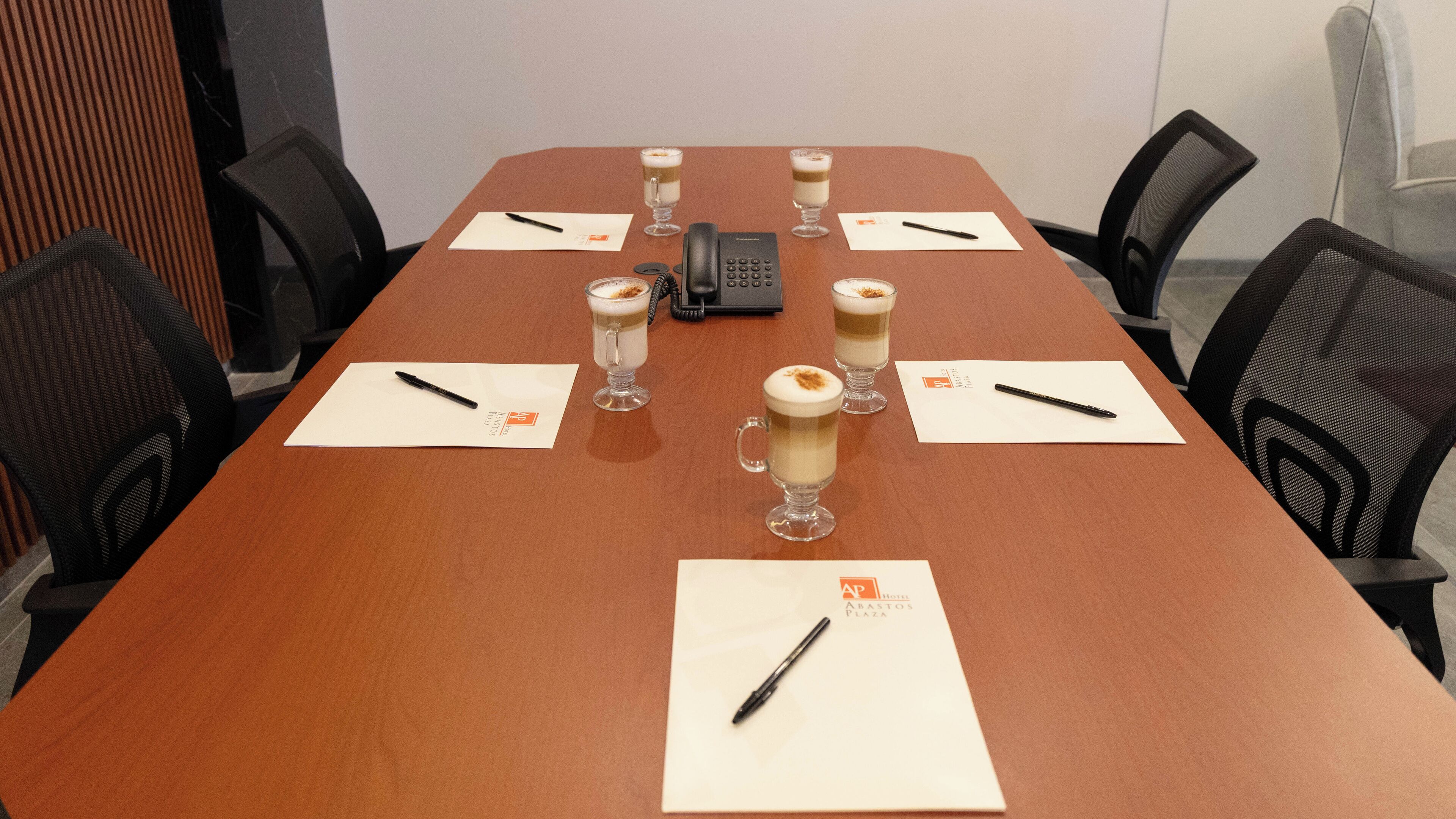 Uma mesa de conferência com quatro xícaras de café, um telefone e canetas sobre guardanapos.