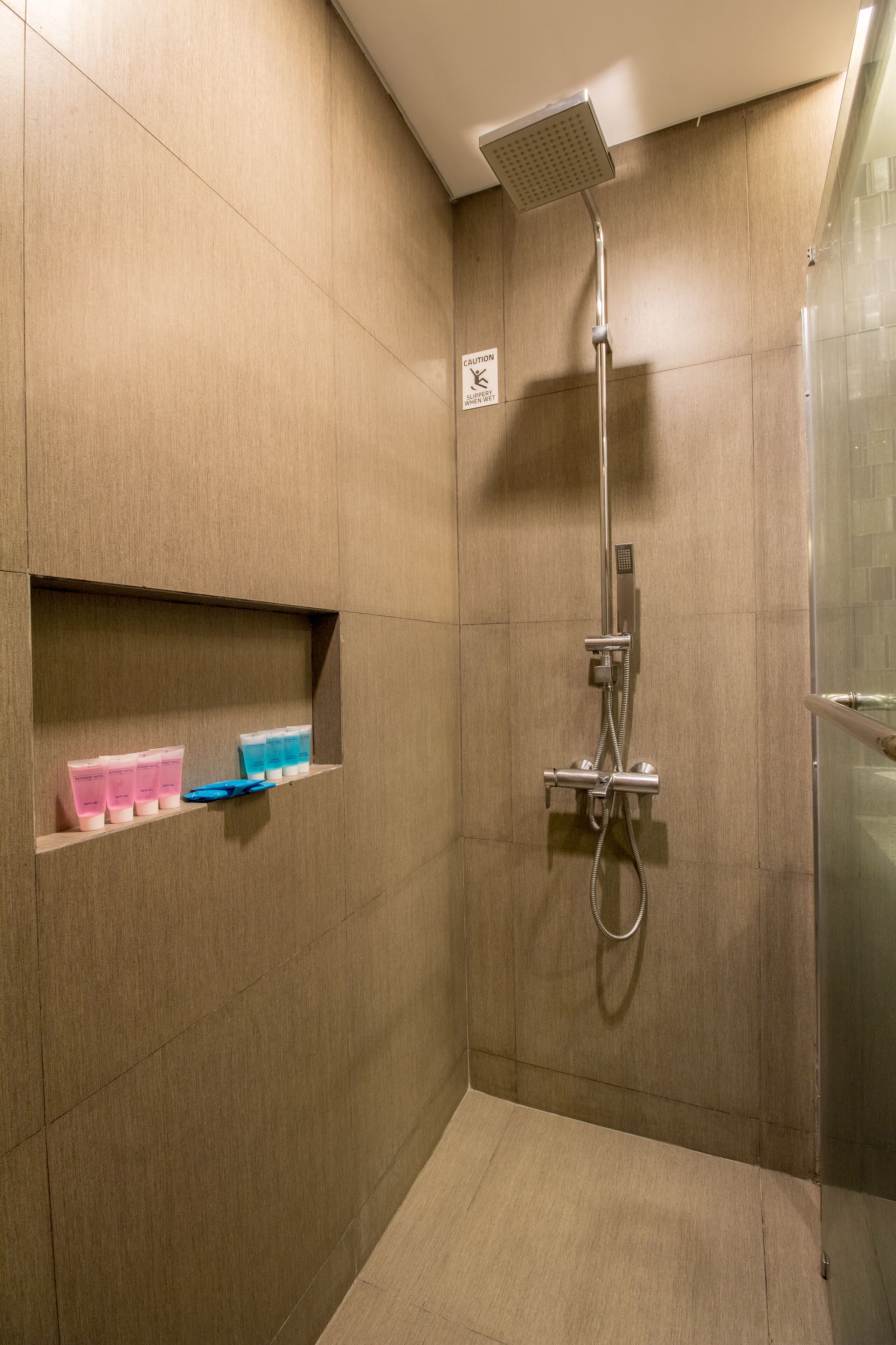 Um chuveiro moderno com chuveiro manual e ducha de teto, um prateleira com artigos de higiene pessoal e um box de vidro.