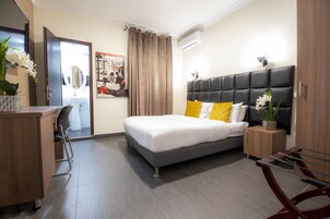 Quarto de hotel moderno com cama, mesa de cabeceira, escrivaninha e uma cadeira.
