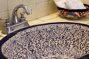 Uma pia de banheiro com uma bacia decorativa, uma torneira e uma parede revestida com azulejos.