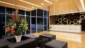 Uma área de recepção moderna com parede de vidro, balcão de atendimento com design geométrico e disposição de assentos.