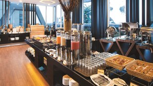 Disposição de buffet com diversos tipos de comida, uma barra de saladas e dispensadores de bebidas.