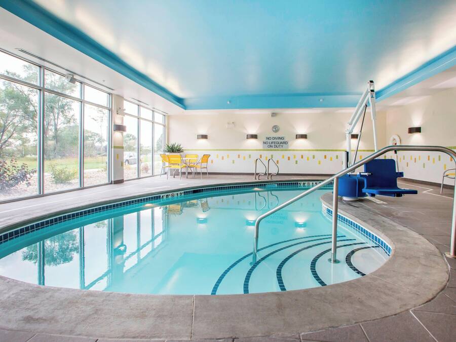 Piscina interna com água azul cristalina, posto de salva-vidas e área de estar com cadeiras amarelas.