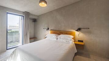 Quarto moderno com cama grande, cabeceira de madeira, mesas de cabeceira e luminária pendente.