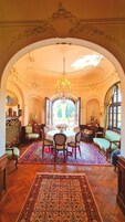 Um quarto ornamentado com um lustre, uma mesa de jantar com cadeiras e uma grande janela com vista para o verde.
