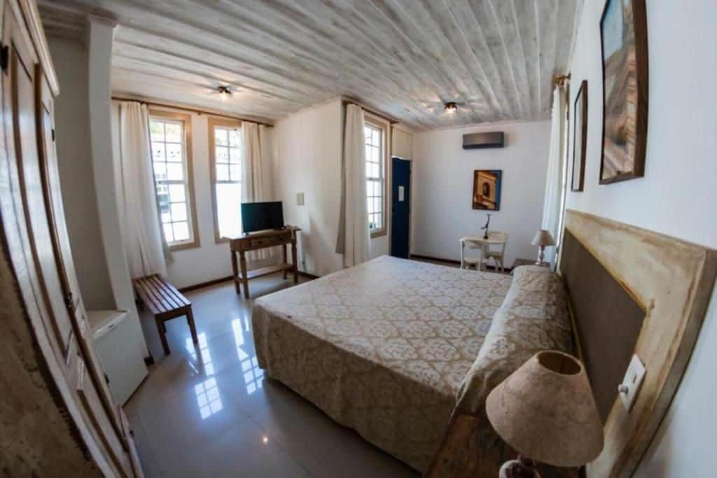 Quarto com cama, escrivaninha, cadeira, televisão e um quadro na parede.