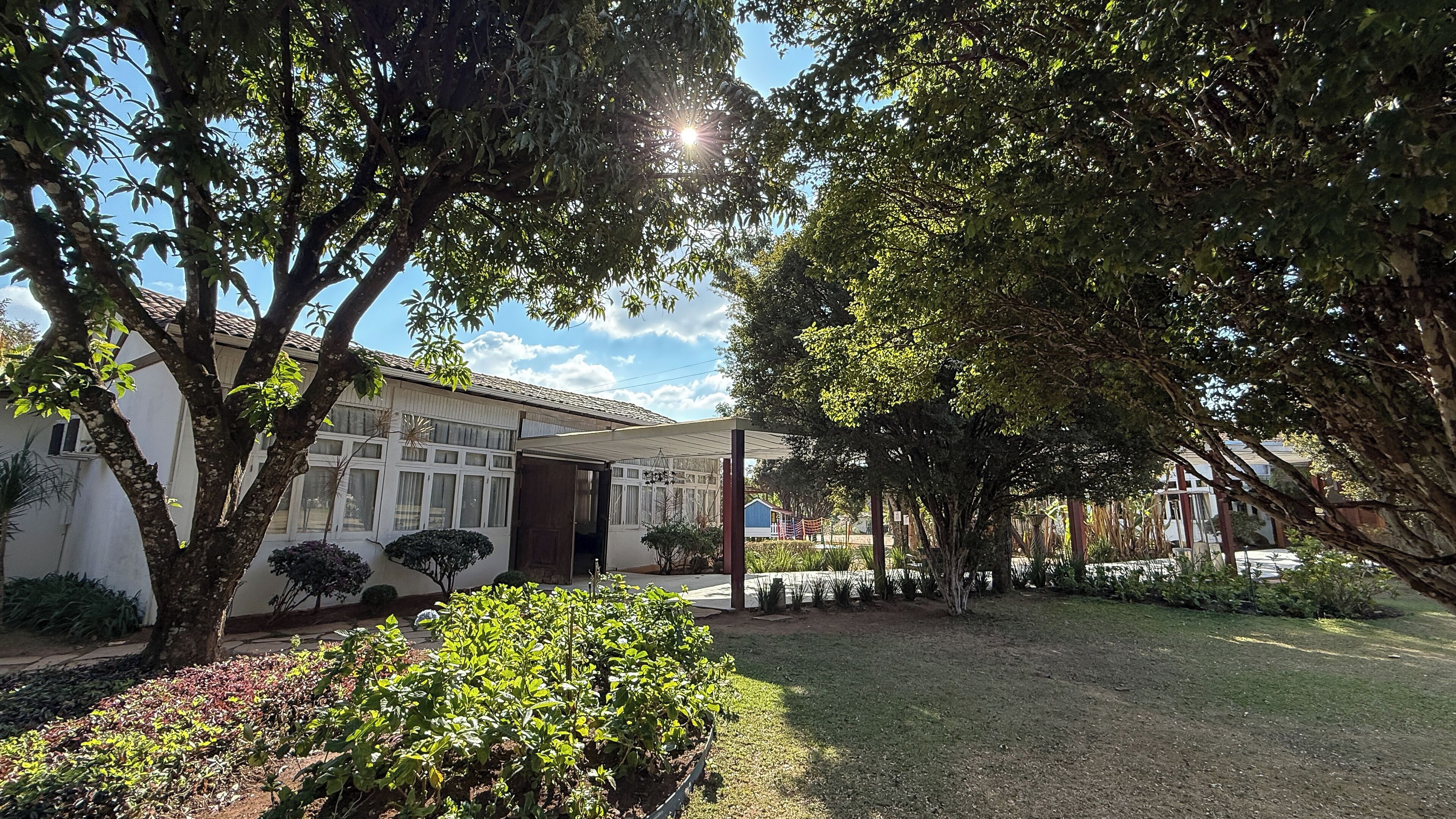 Um imóvel residencial com um alpendre coberto, um jardim com diversas plantas e uma casa com telhado ladrilhado e paredes brancas.