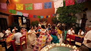 Um pátio com pessoas jantando em mesas, cercado por decorações coloridas e uma fonte.