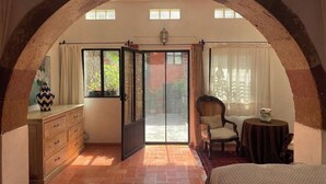 Um quarto com uma grande porta arqueada, uma cama, uma cadeira, uma mesa pequena e um aparador.