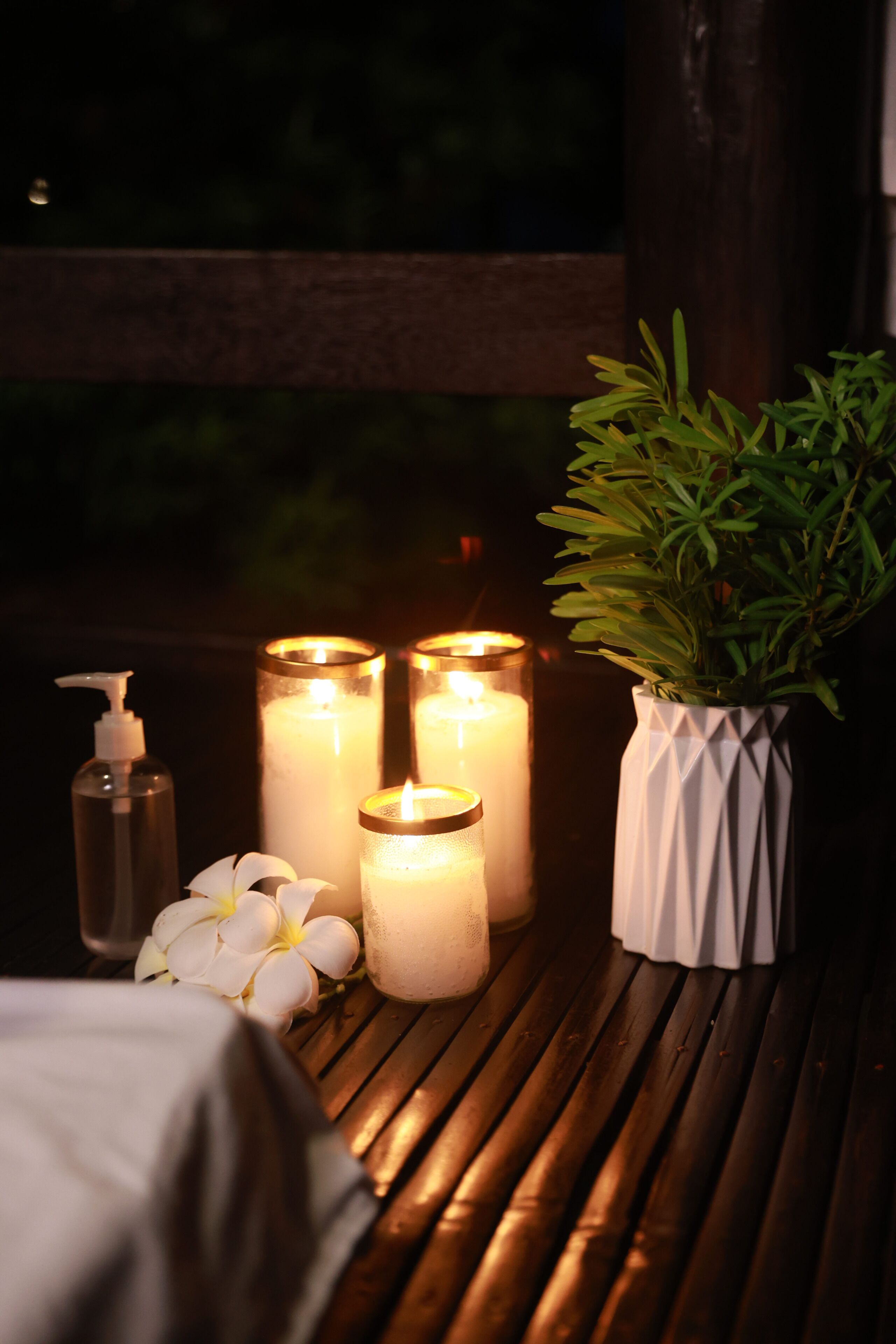 Um deck de madeira com velas, um vaso de planta e uma garrafa de loção.