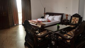 Quarto de hotel com cama, escrivaninha e duas cadeiras. Possui janela com cortinas, aparelho de ar condicionado e luminária fixada na parede.
