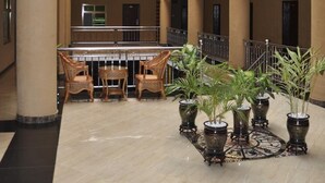 Um átrio com vários níveis, área de estar central, plantas em vasos e guarda-corpo decorativo.