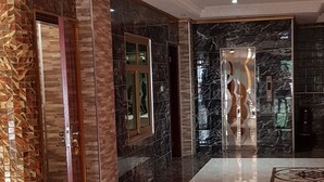Um hall amplo com piso de mármore, um elevador de vidro e uma parede decorativa com design padronizado.