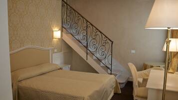 Quarto de hotel com cama, poltrona, escrivaninha, luminária e escada com corrimão decorativo.