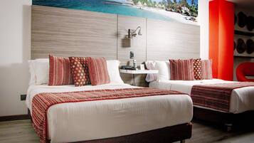 Quarto de hotel com duas camas, uma luminária na parede, uma mesinha e um mural com tema praiano.